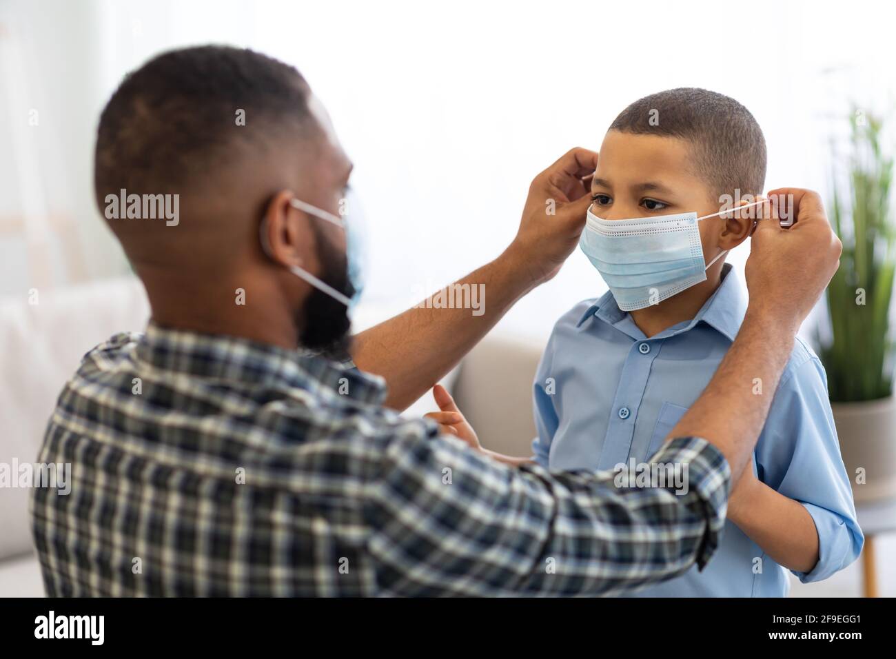 Careful African Father Putting Face Mask On Son Indoors Stock Photo - Alamy