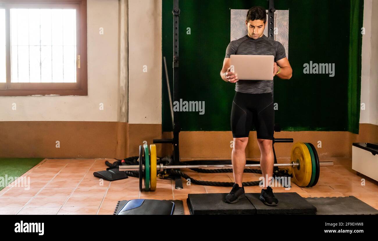 Latino coach in sportswear working out in gym with computer preparing ...