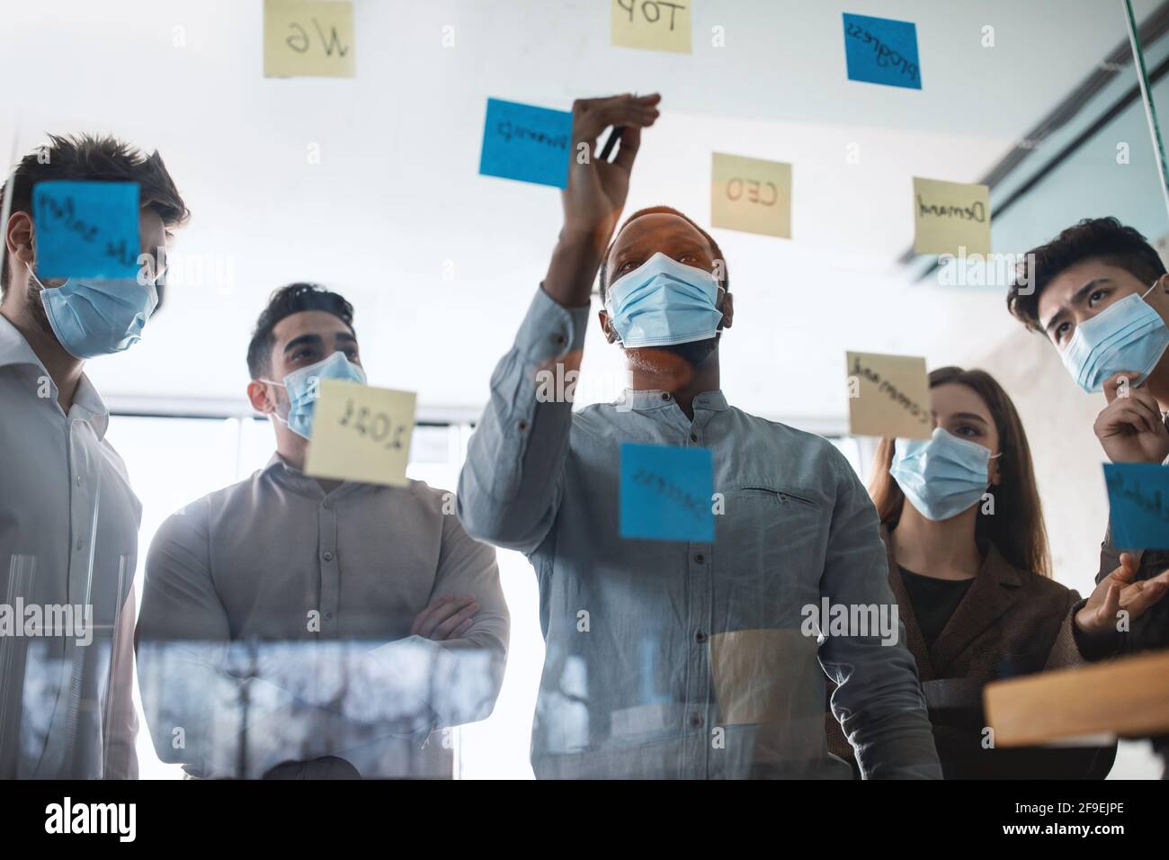 Businesspeople having meeting using sticky post-it notes on glass wall ...