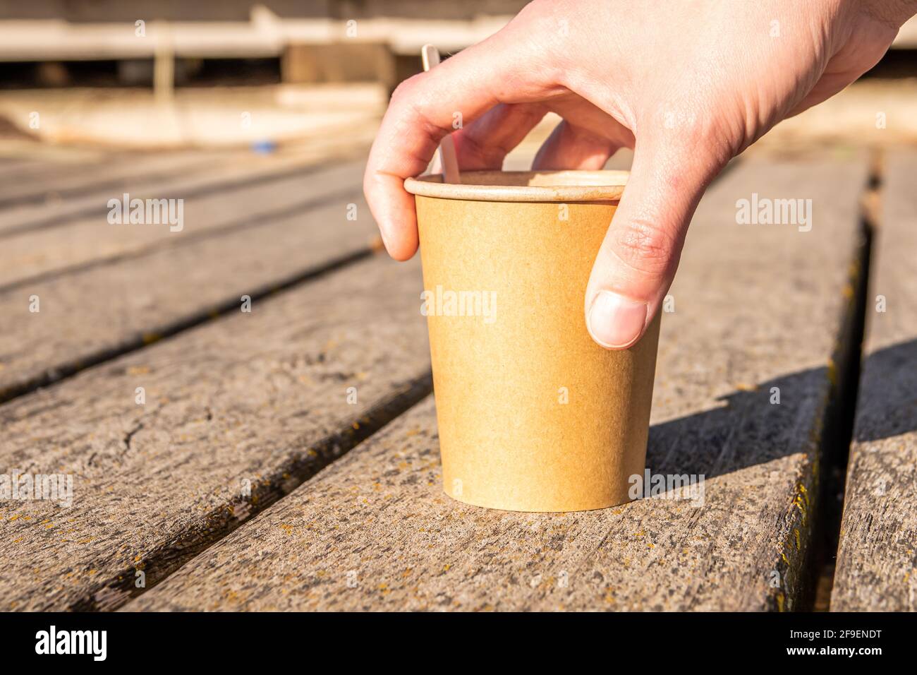 A closeup shot of a male hand holding a paper cup of coffee on a wooden ...