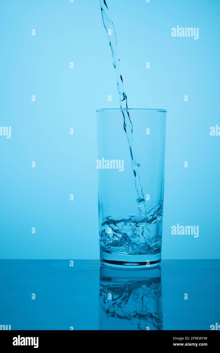 Pure still water pours from bottle to glass against blue background ...