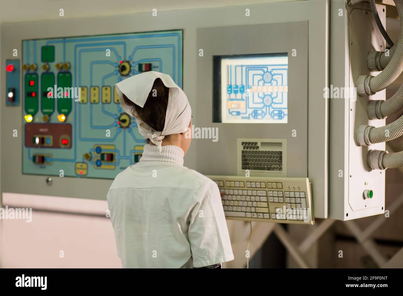 Back view of female worker at machine control panel at manufacturing ...