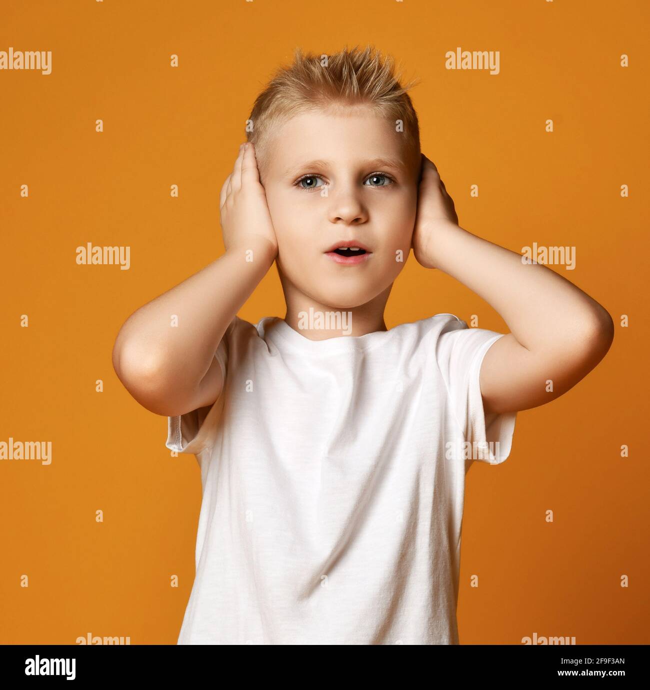 Blond boy child in white t-shirt and jeans standing and covering his ...
