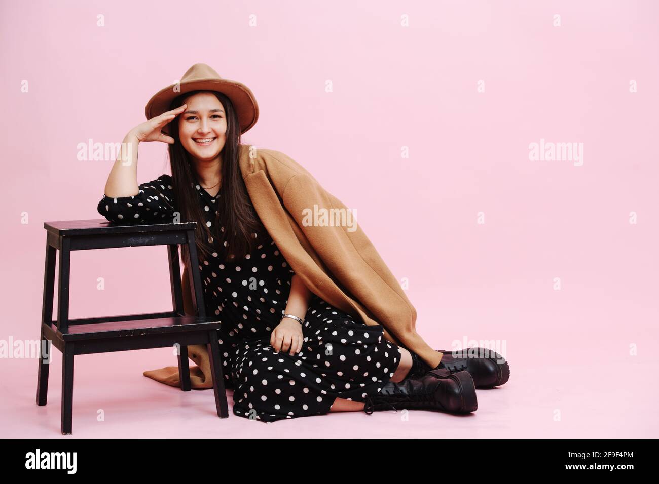 Happy smiling young woman sitting on the floor, leaning on a stool ...