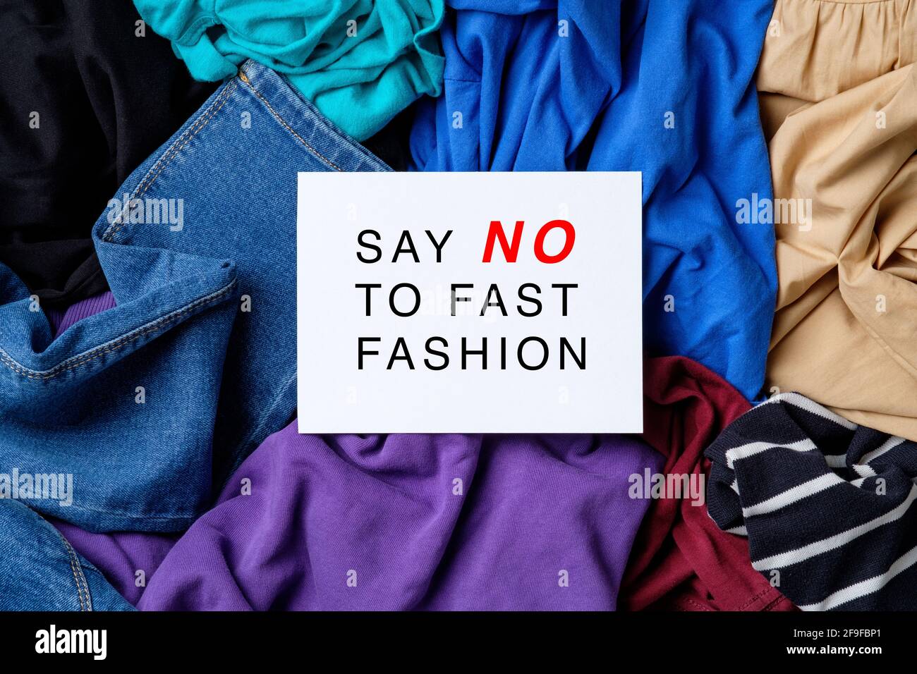Say NO to fast fashion sign on white paper over heap of female clothes ...