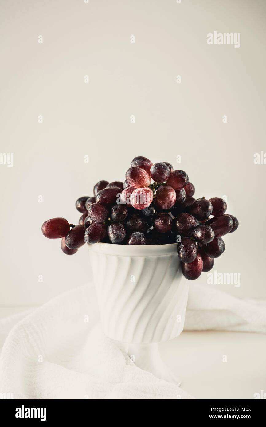 Dark red grapes in an old white porcelain bowl standing on a white ...
