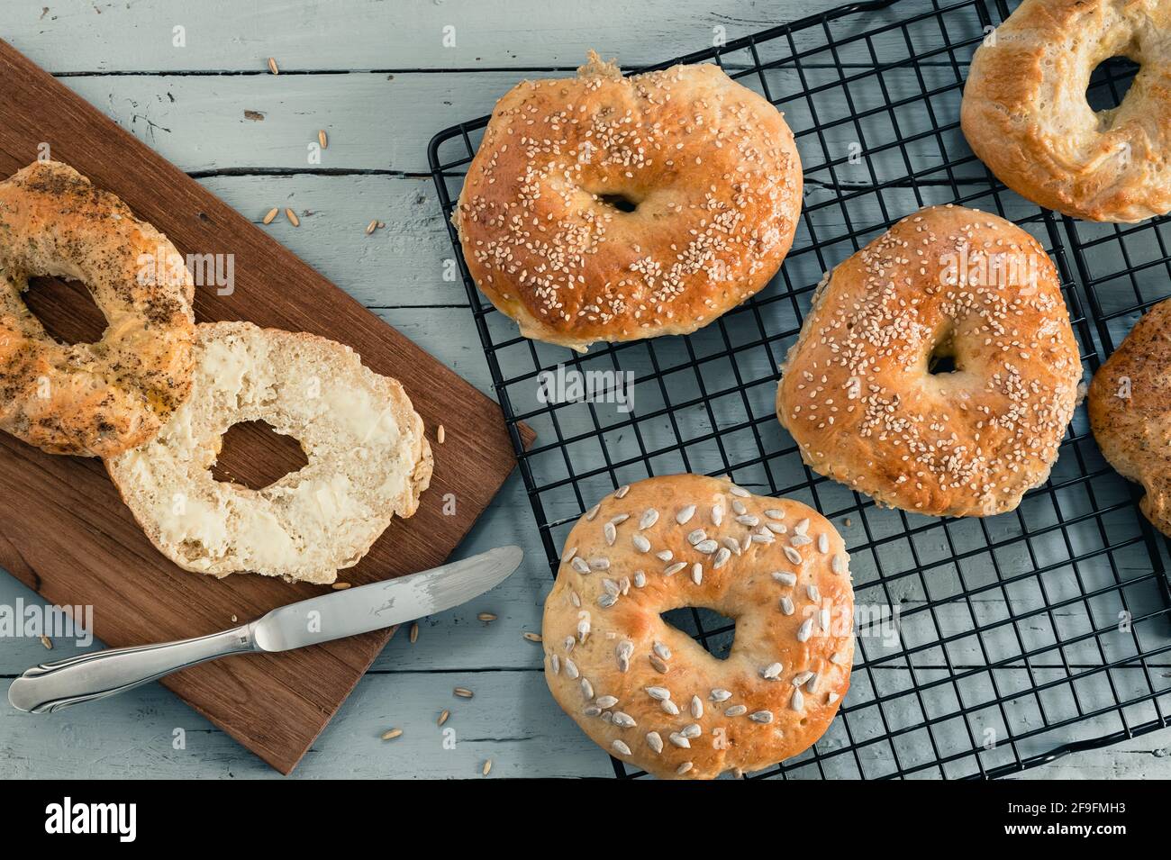 Homemade bagels on a cooling rack on grey wood, one with butter on a ...