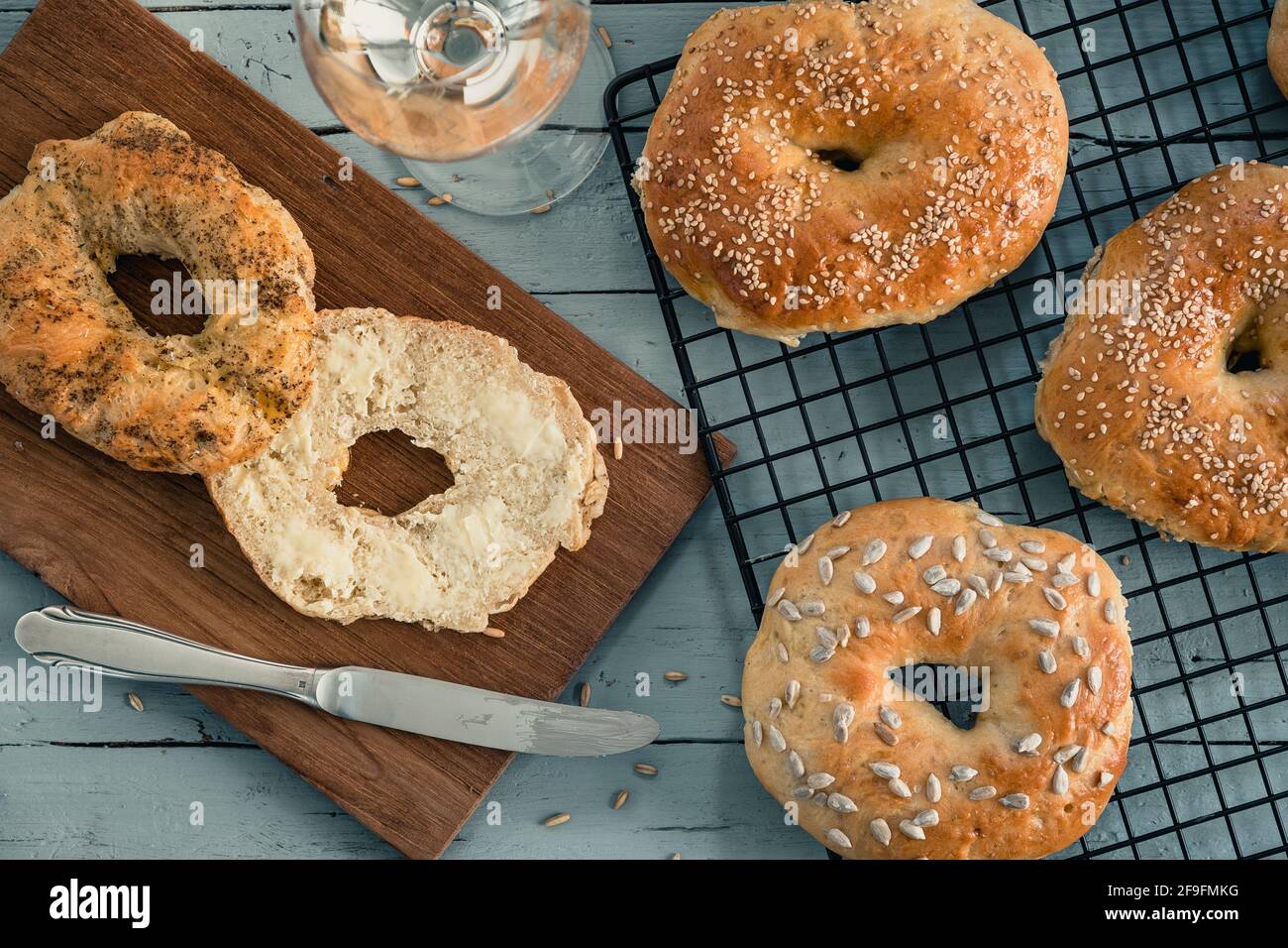 Homemade bagels on a cooling rack on grey wood, one with butter on a ...