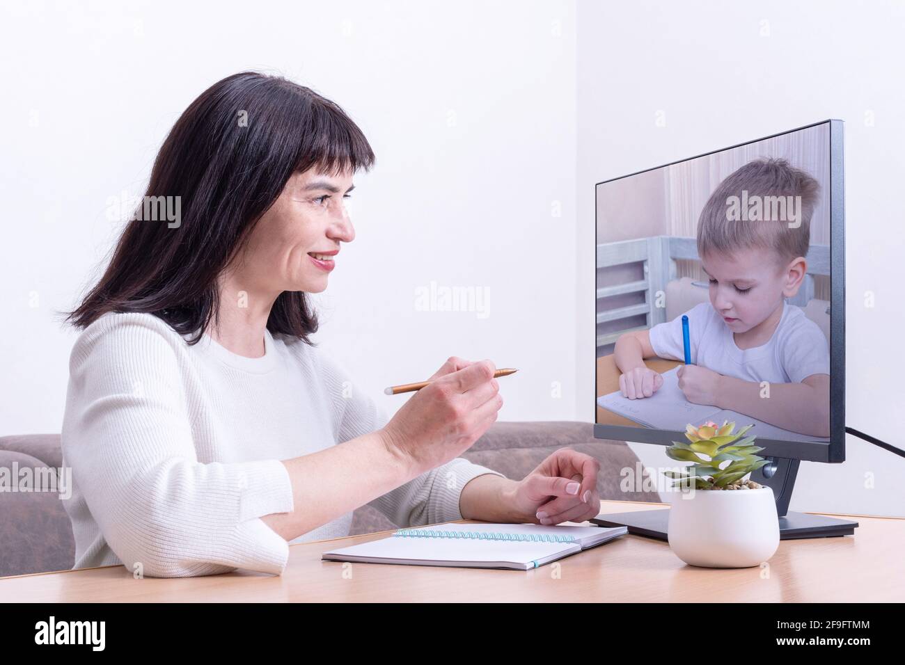 A female teacher sitting in front of a computer monitor holds a pen and ...