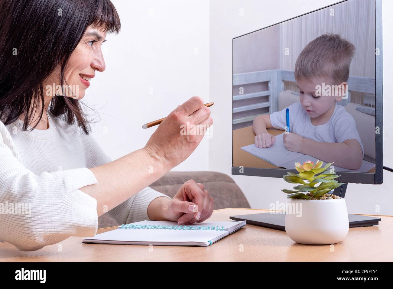 Attractive female teacher sitting in front of a computer monitor holds ...