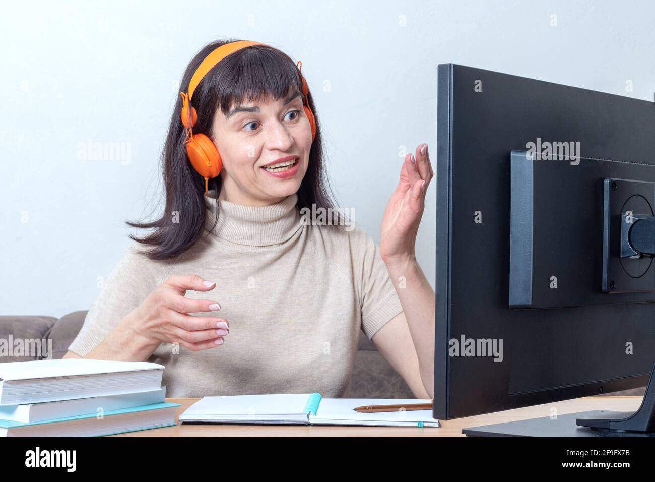 An attractive female teacher in orange headphones sitting in front of a ...
