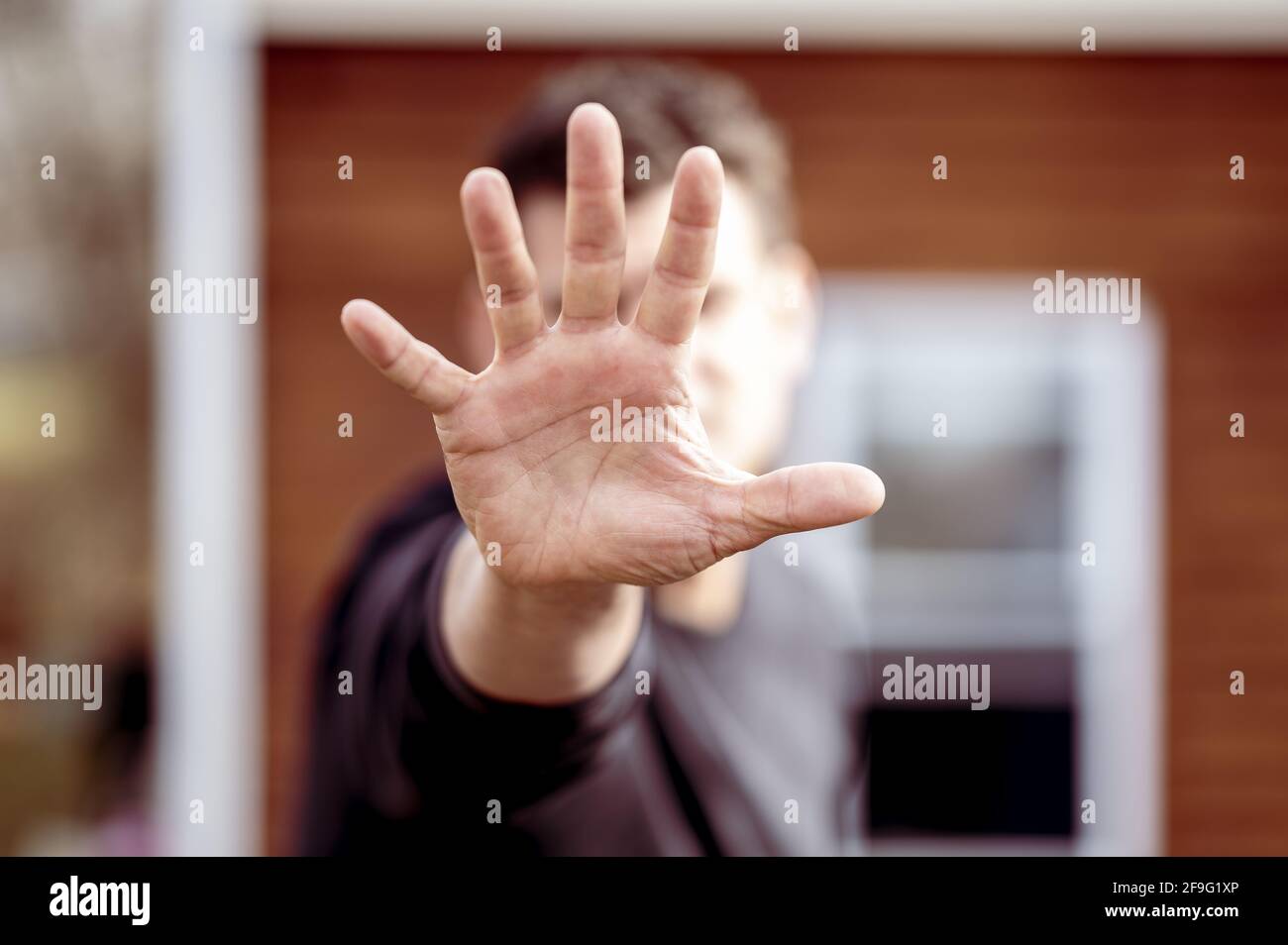 A shallow focus of a young Caucasian man doing the stop sign with his ...
