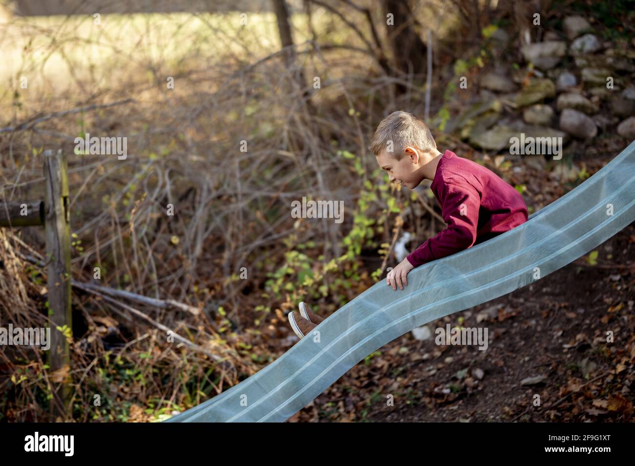 A blonde boy sliding down a playground slide Stock Photo - Alamy