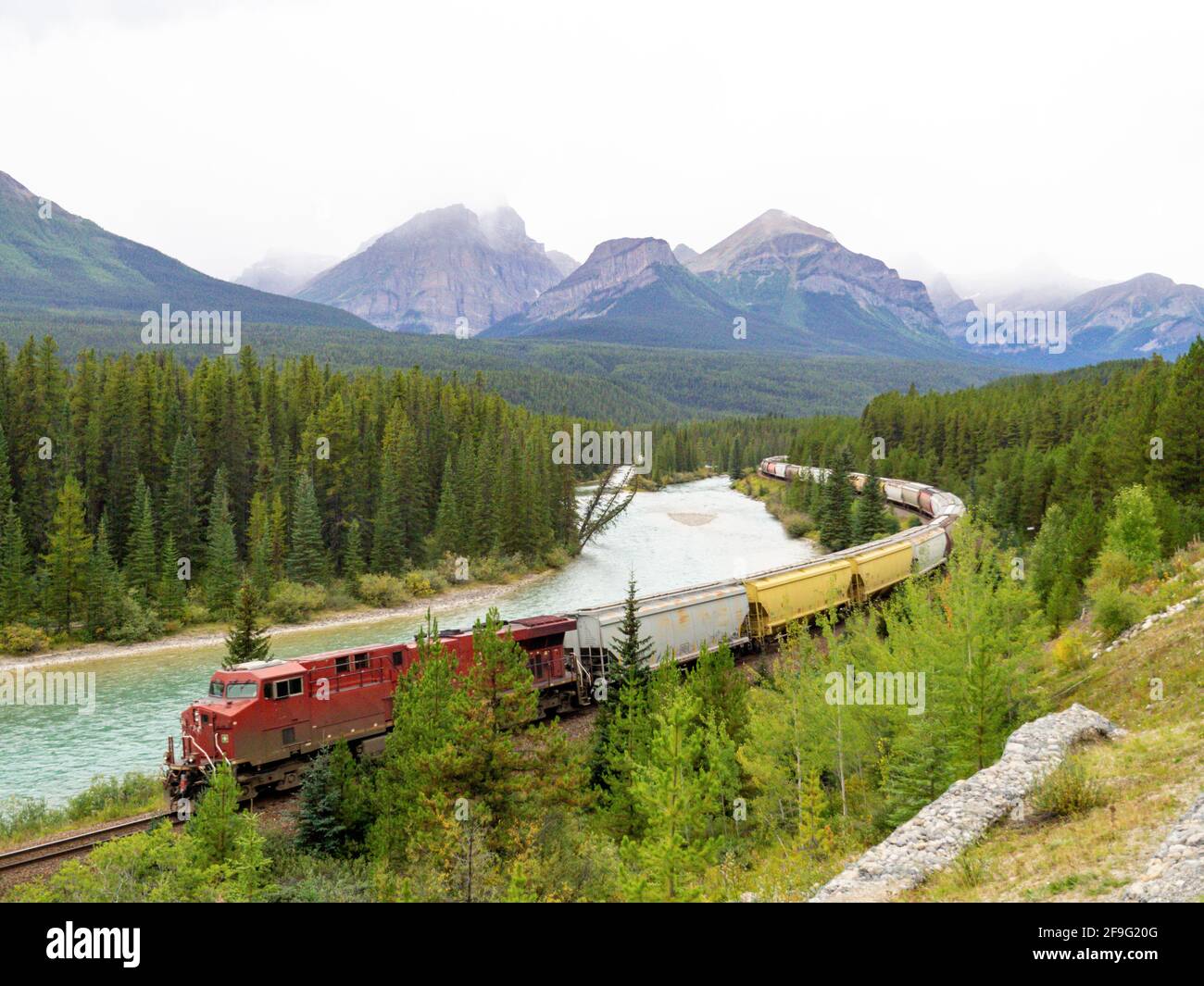 red cargo train following the curve of the railroad next to a river in ...