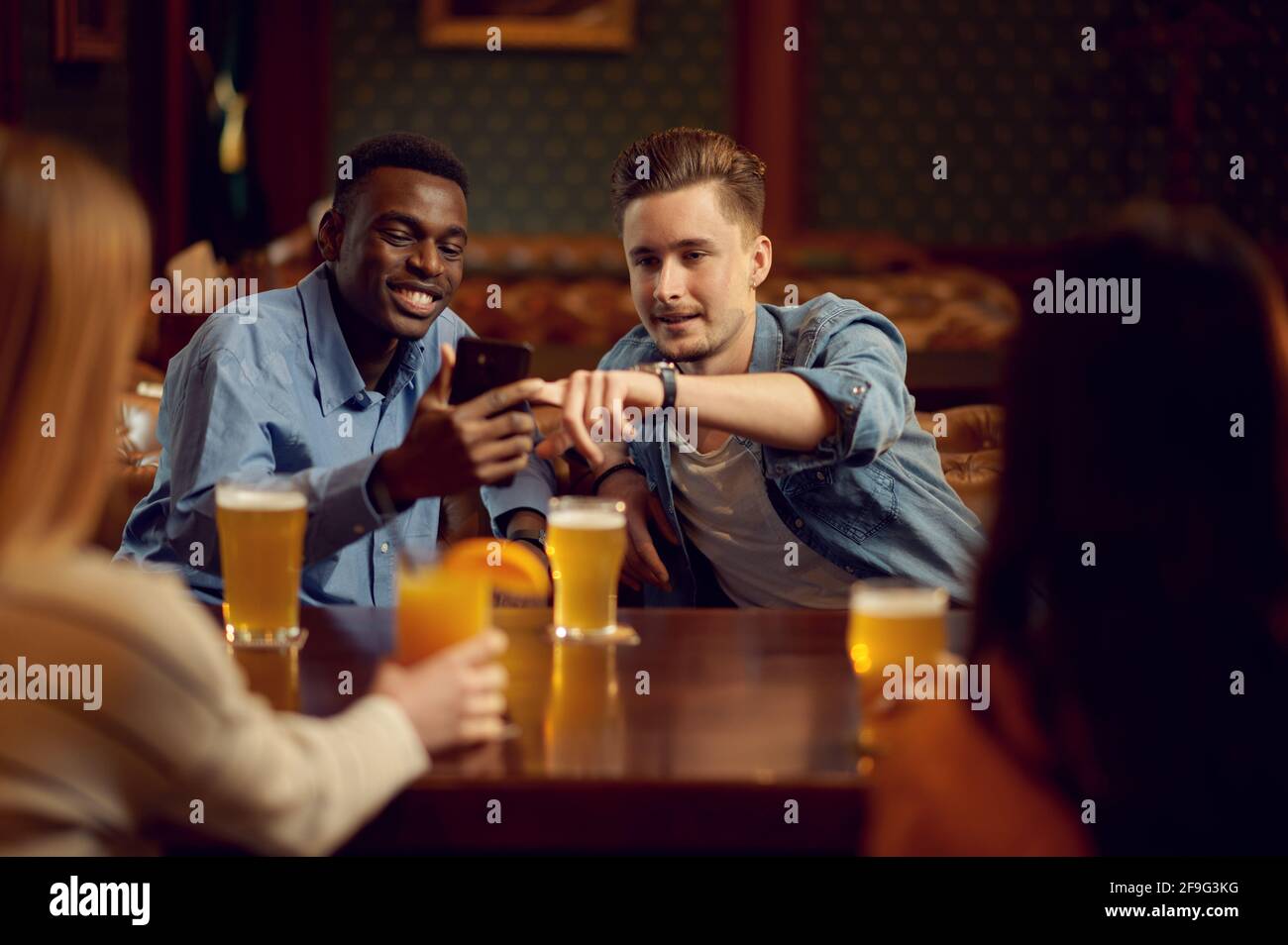 Four friends drinks alcohol at the table in bar Stock Photo - Alamy