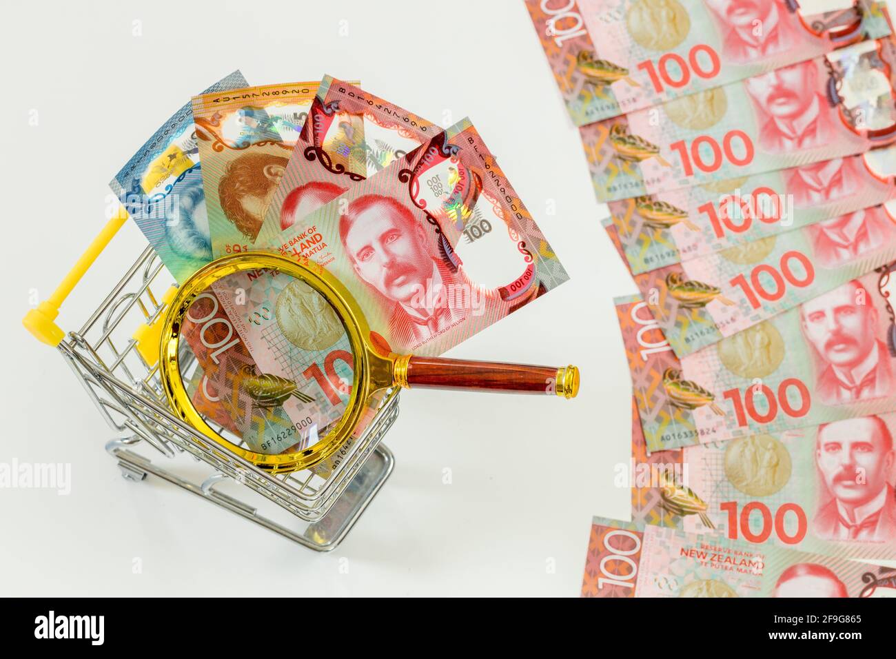 A miniature shopping cart with New Zealand dollars and a magnifying ...