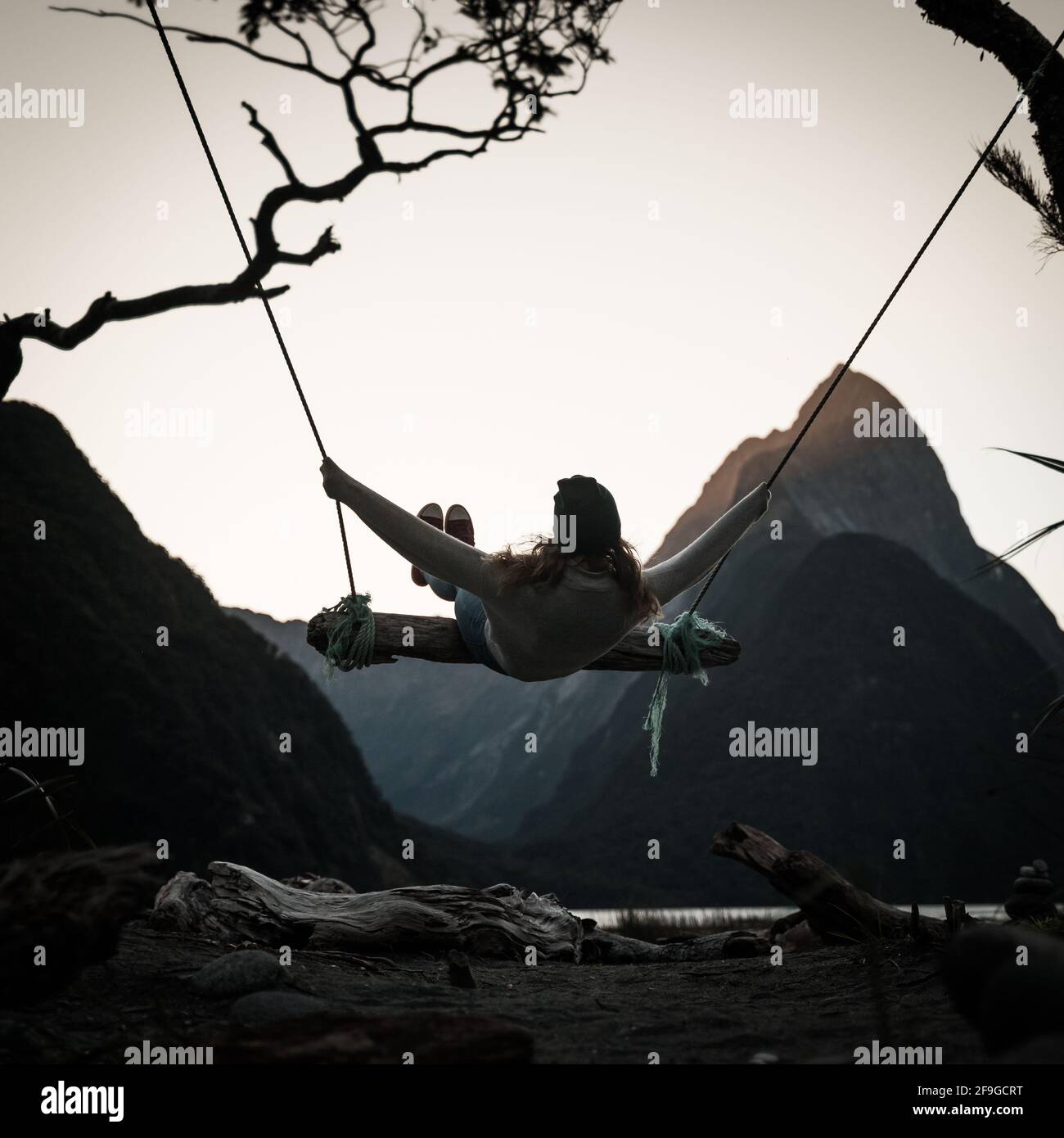 A back view of a young girl on a swing facing a beautiful landscape of ...
