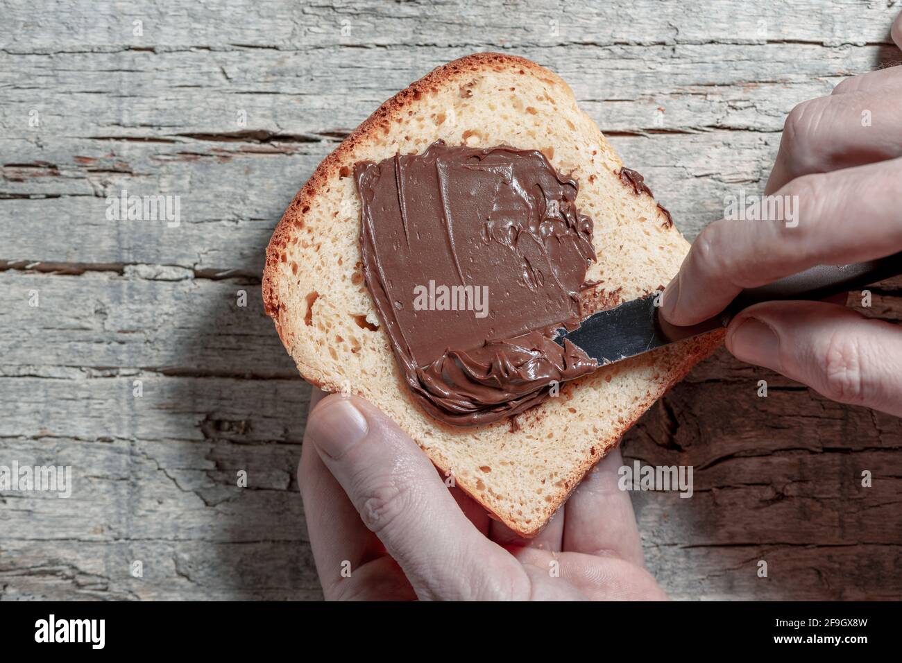 A top view of a hand spreading a chocolate spread on a bread slice ...