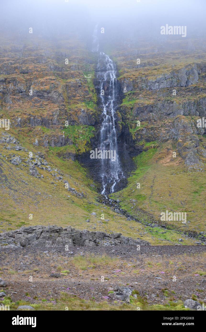 A stunning view of a tall thin waterfall among grassy cliffs lost in ...