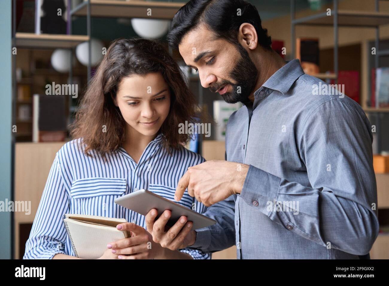 Indian manager and young latin employee talking in office using tablet ...