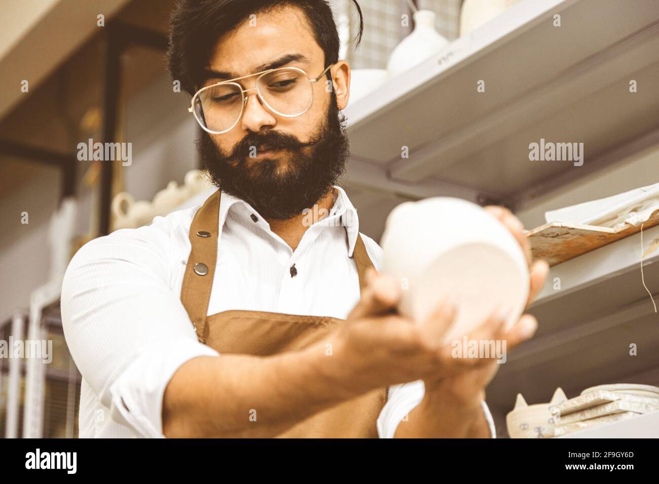 A young attractive male potter with a beard and mustache works in his ...