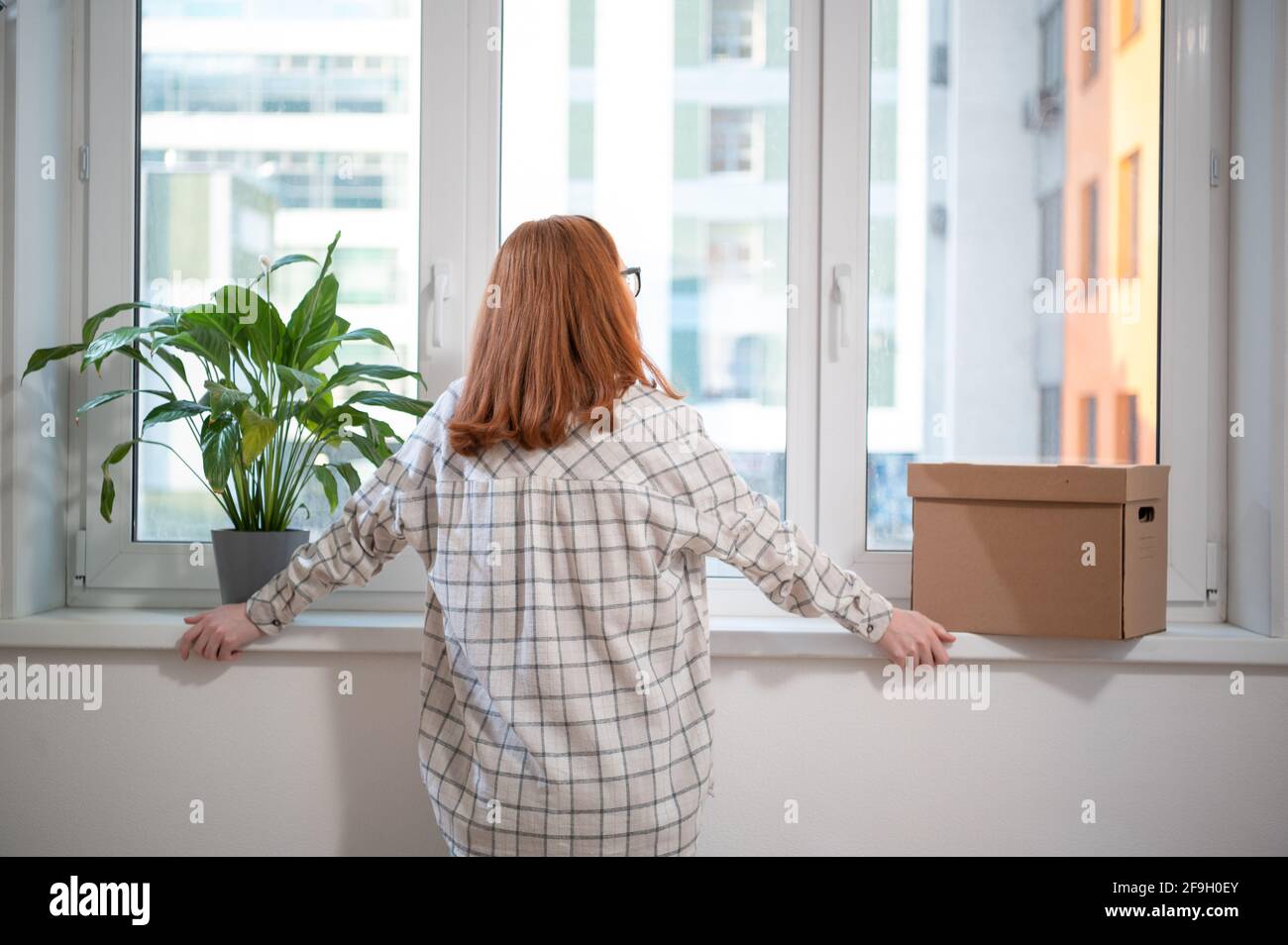 A young woman admires the view from the window in her new apartment in ...