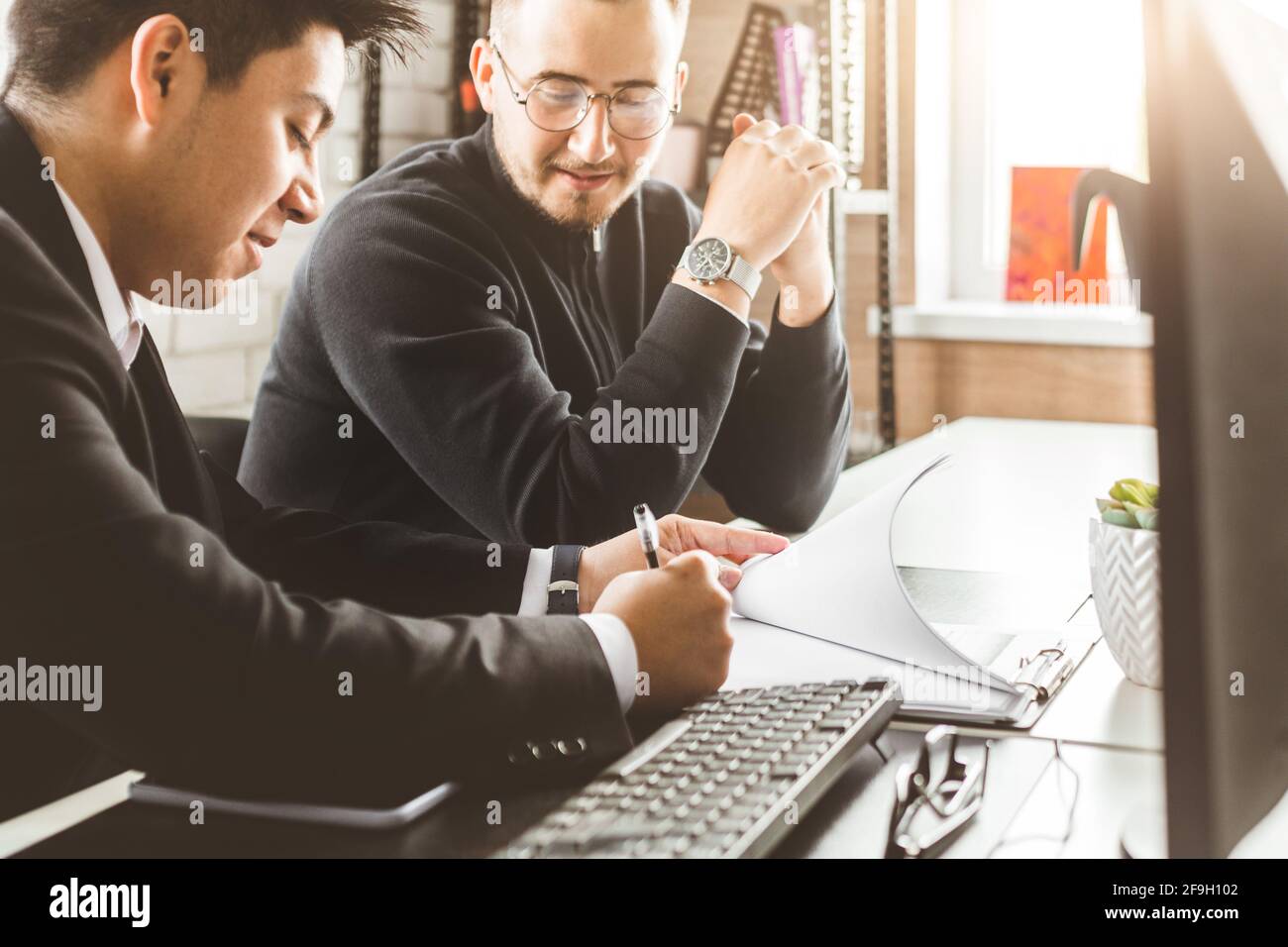 Young office worker sitting at desk, using computer. Two business man ...