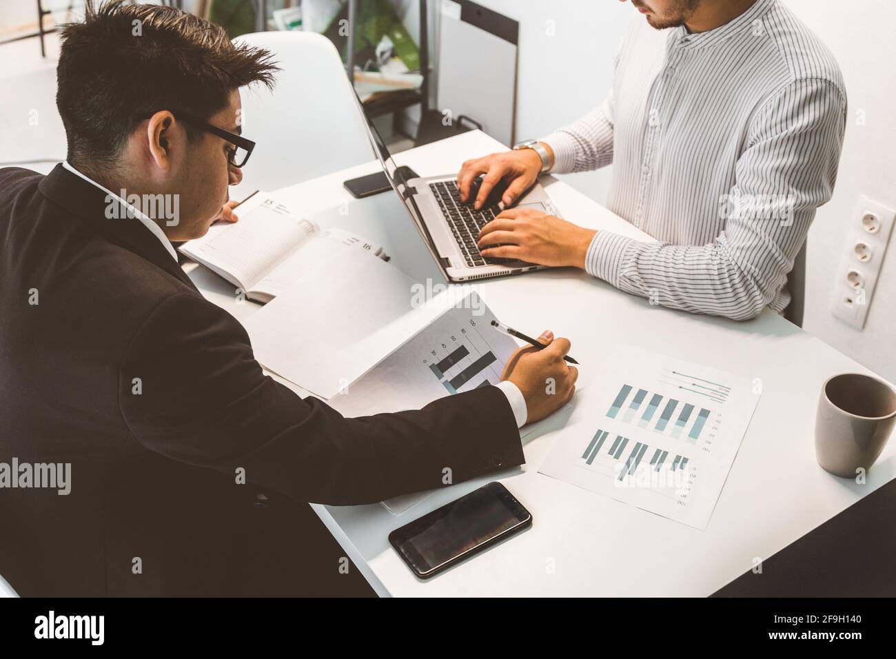 Young office worker sitting at desk, using computer. Two business man ...