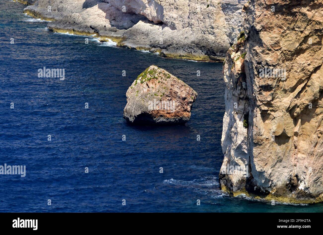 A small boulder islet or mini island at the foot of steep cliffs in ...