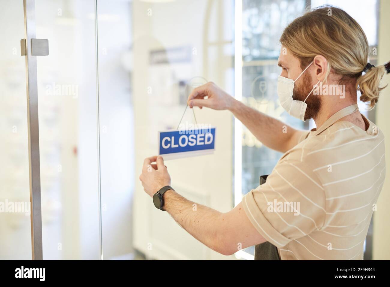 Side view portrait of man hanging CLOSED sign on glass door in cafe and ...