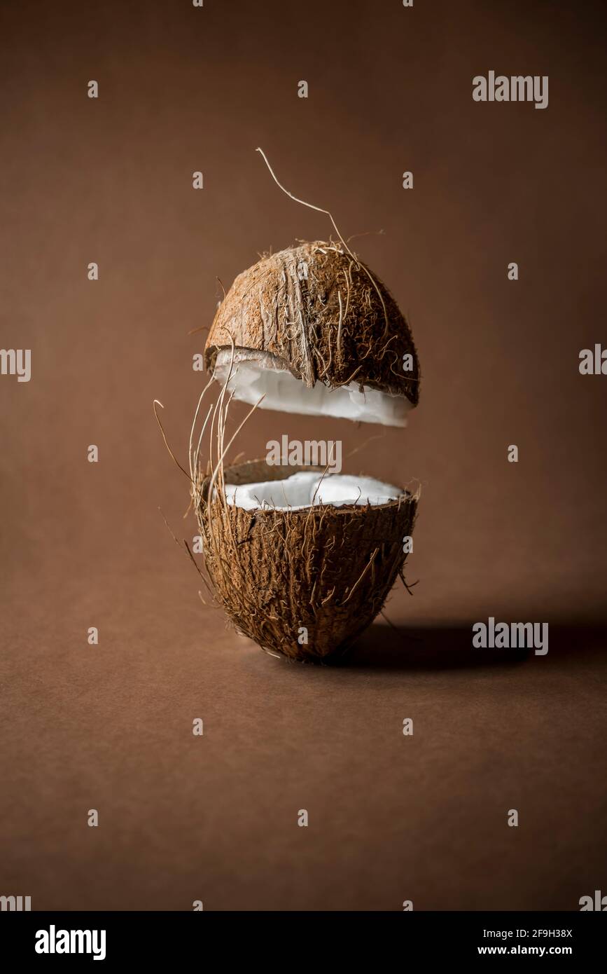 Floating coconut sliced in half on a sandy brown background. Minimal ...