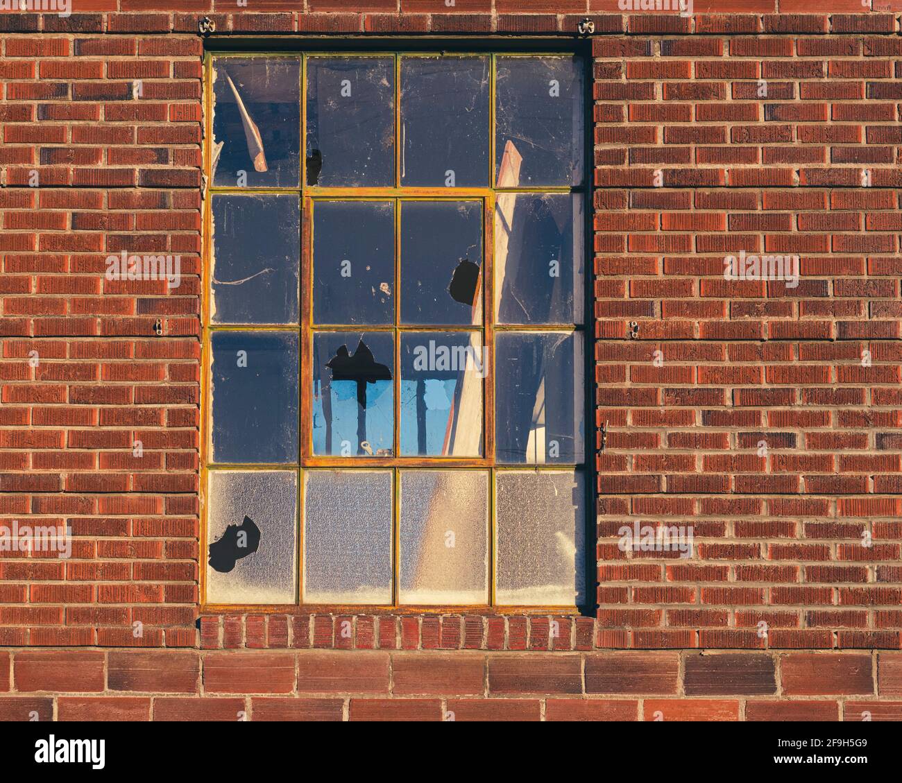 Blue sky shows through a broken window of a vacant red brick building ...