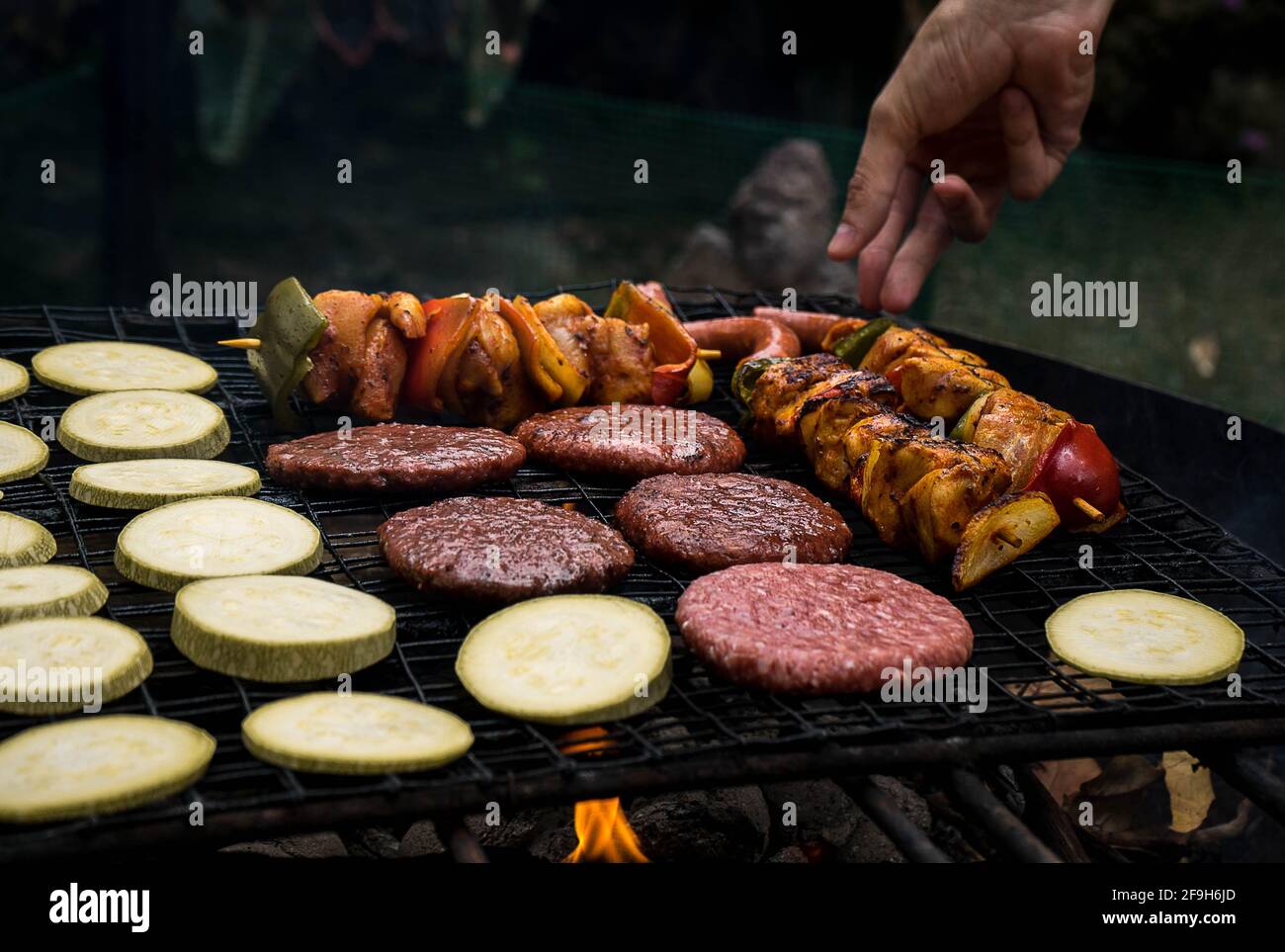 Closeup shot of a hand turning grilled meat and vegetables on the ...