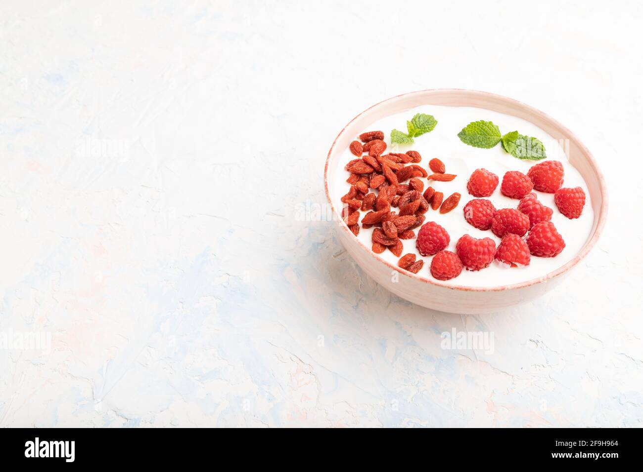Yogurt with raspberry and goji berries in ceramic bowl on white ...