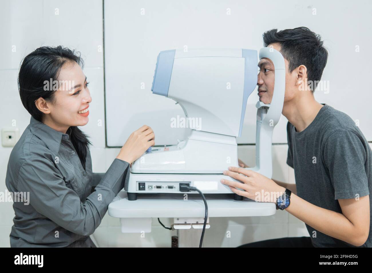 a female doctor and a male patient doing an eye check using a device ...