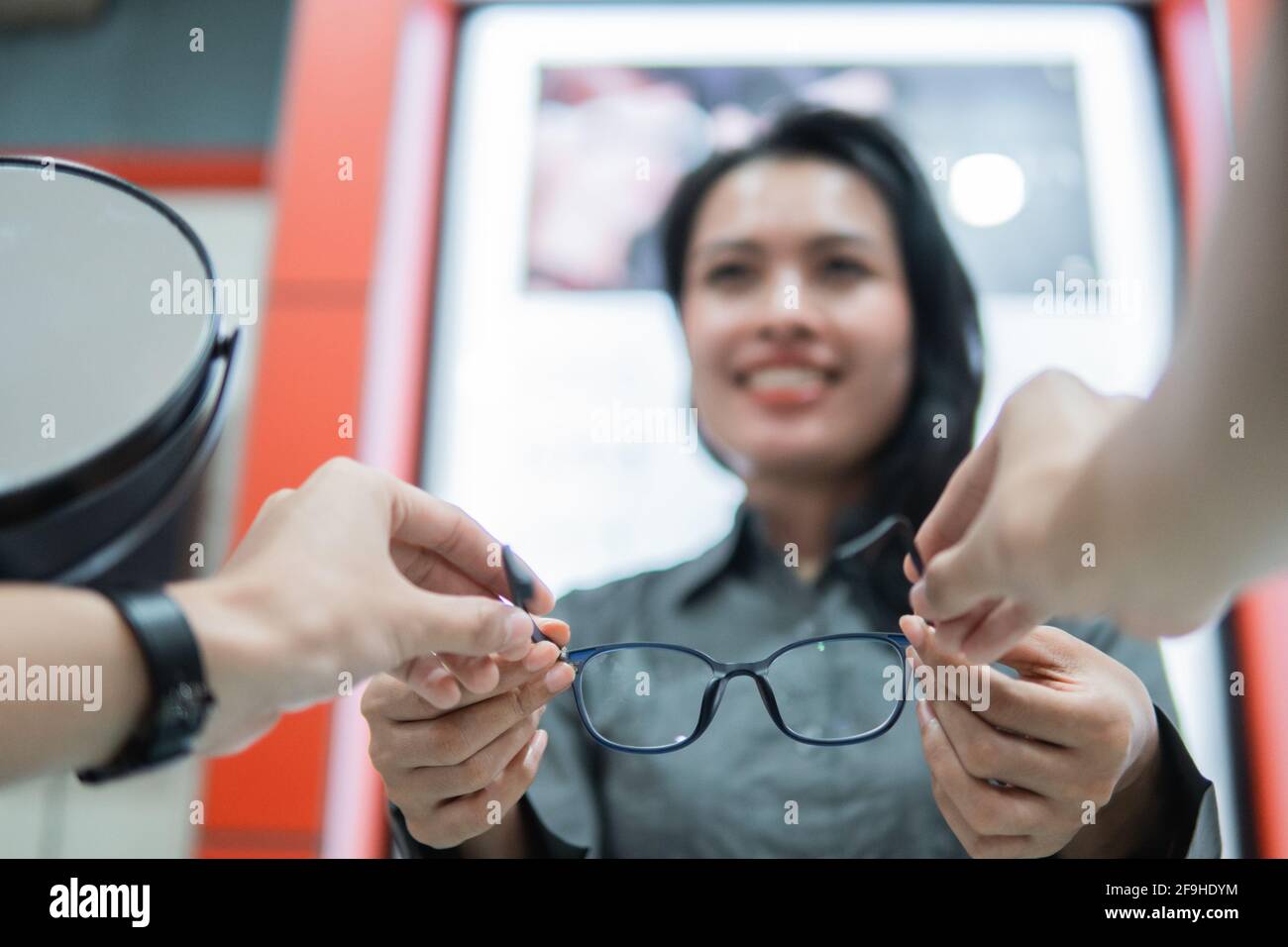 selective focus of a beautiful shop assistant giving a pair of glasses ...