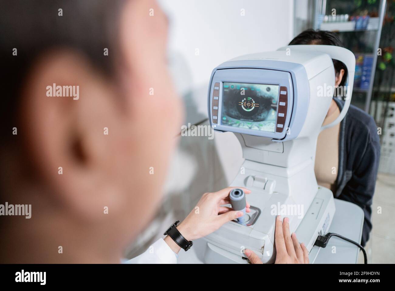 a male ophthalmologist is operating an eye computer for a female ...