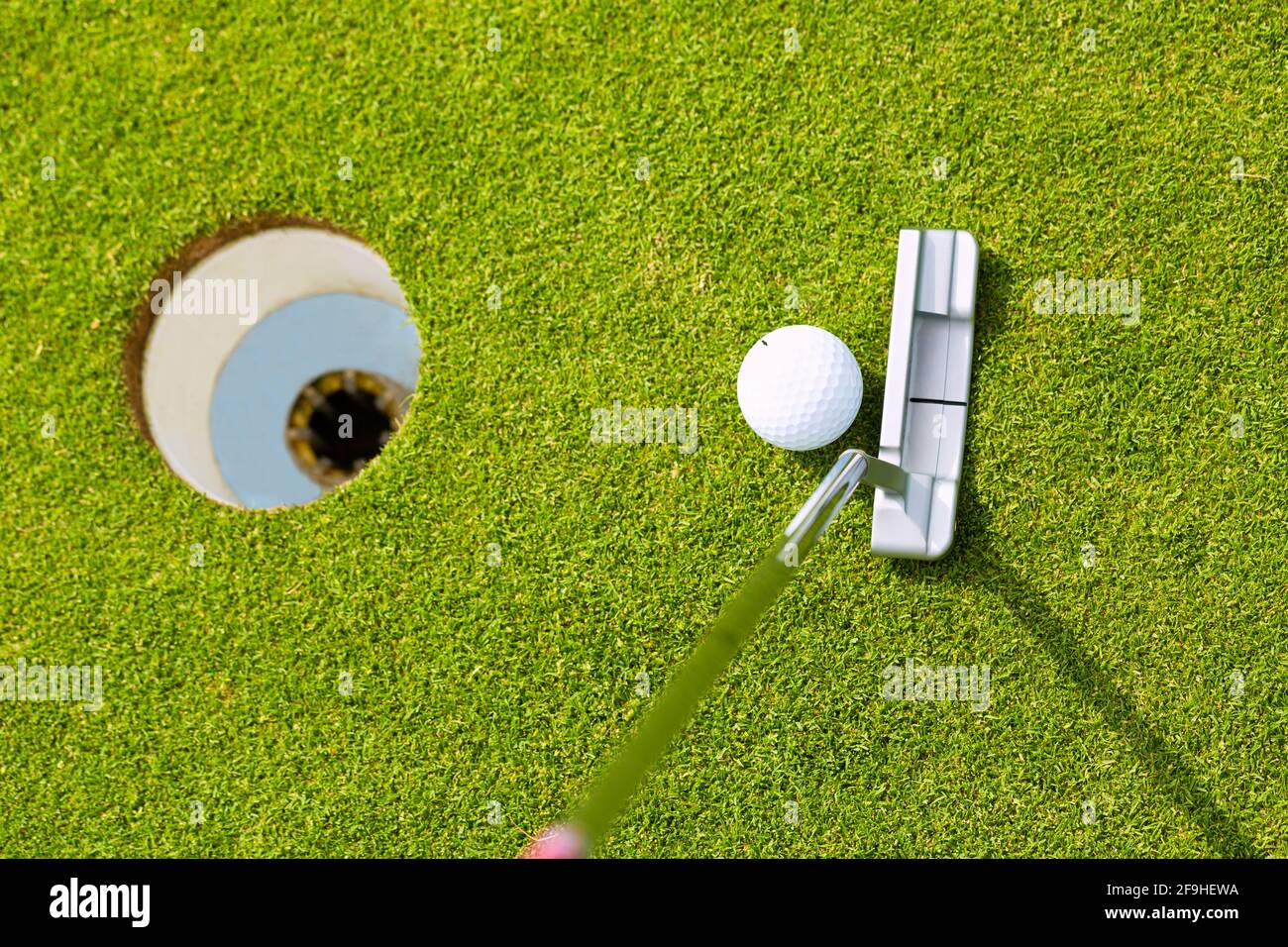 Golf player putting ball into hole, only ball, hole and iron to be seen ...