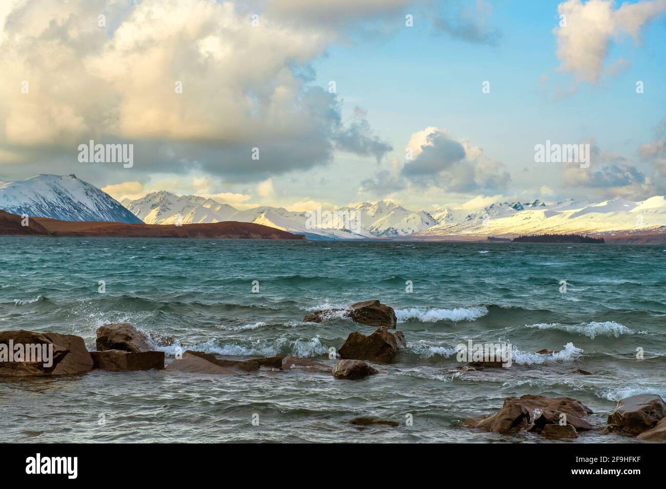 Rocks in turquoise water, waves in Lake Tekapo, background is Mount ...
