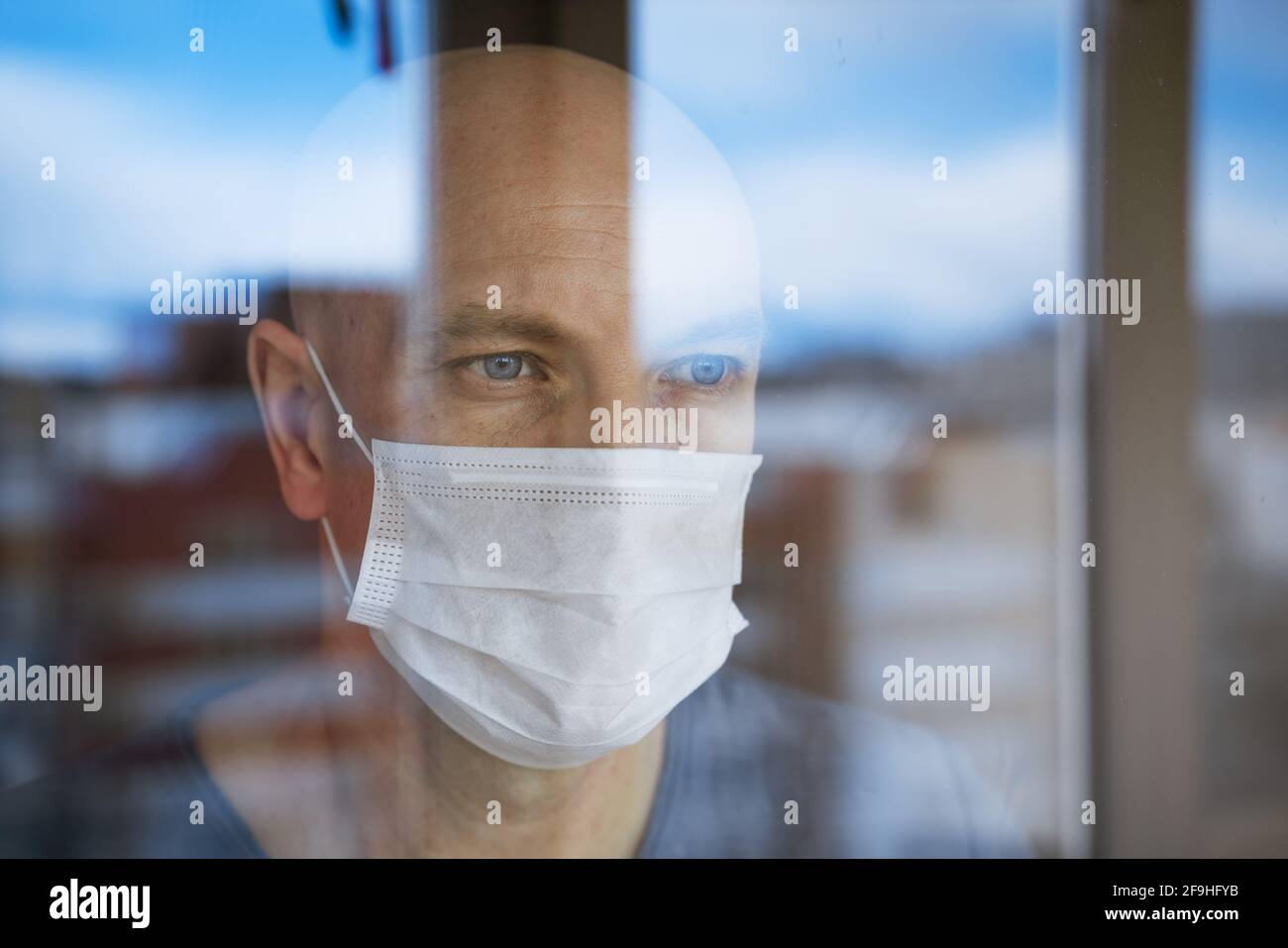 portrait of a bald man in a protective mask looking through the windows ...
