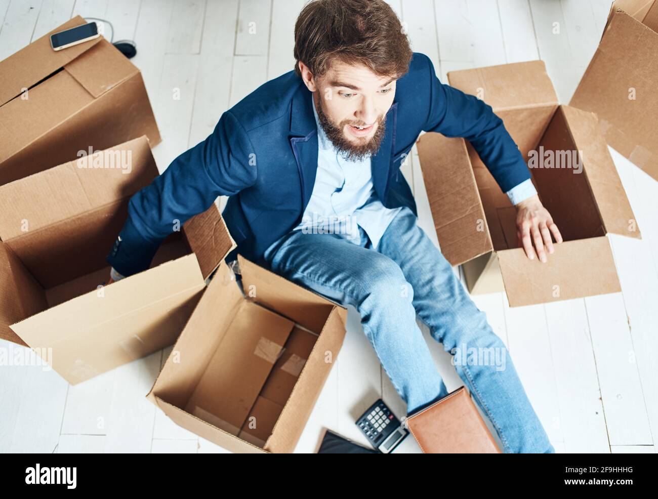 Business man with boxes sits on the office floor unpacking things Stock ...