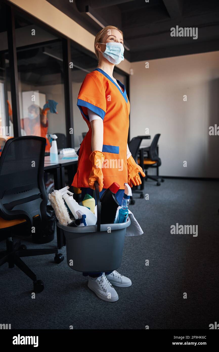 Janitor with cleaning products in her hands looking into the distance ...