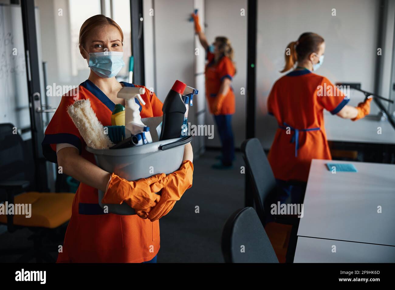 Female janitor with cleaning products standing among her busy ...