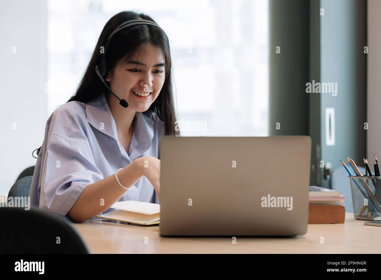 Asian young female student sitting while using headphones and laptop ...
