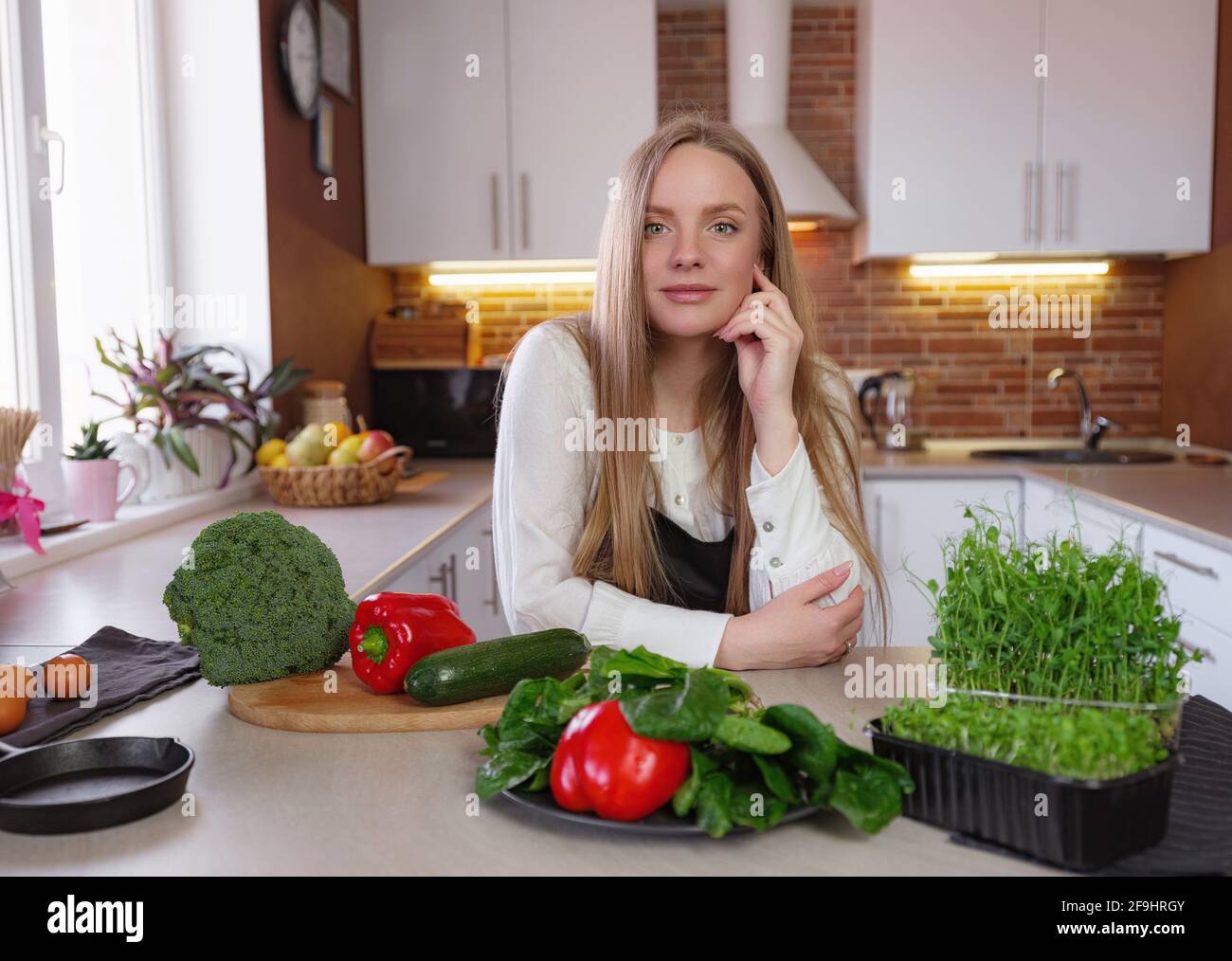 A young blonde happy lady standing in the kitchen while cooking healthy ...