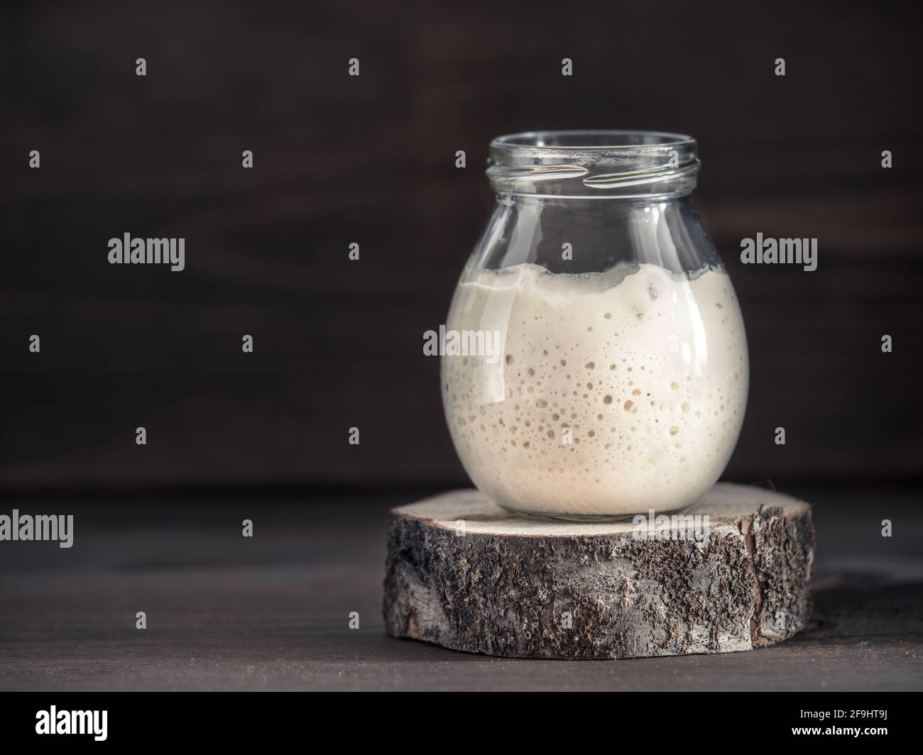 Active wheat sourdough starter in glass jar on brown wooden background ...