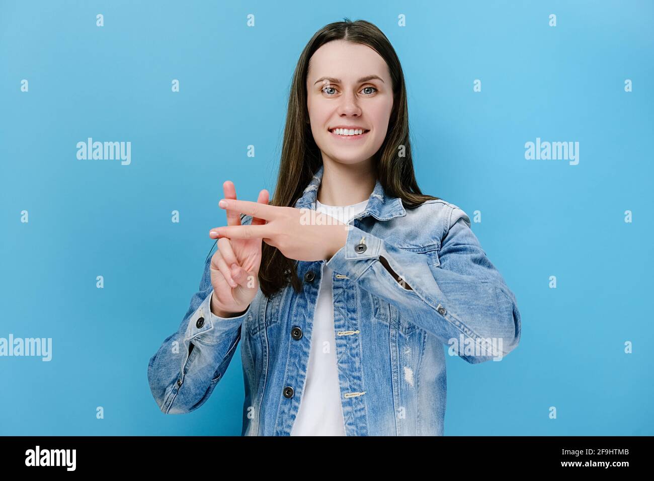 Charming young woman crossing fingers to make hashtag sign and looking ...