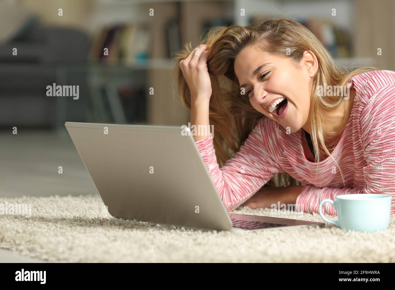 Funny woman laughing loud watching media on laptop lying on the floor ...