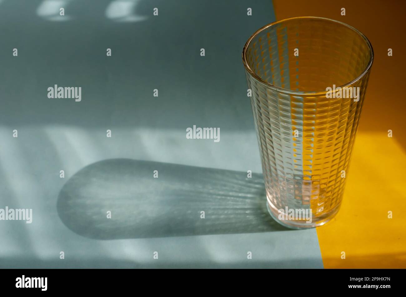 Minimalist light and shadow composition with an empty glass on a yellow ...