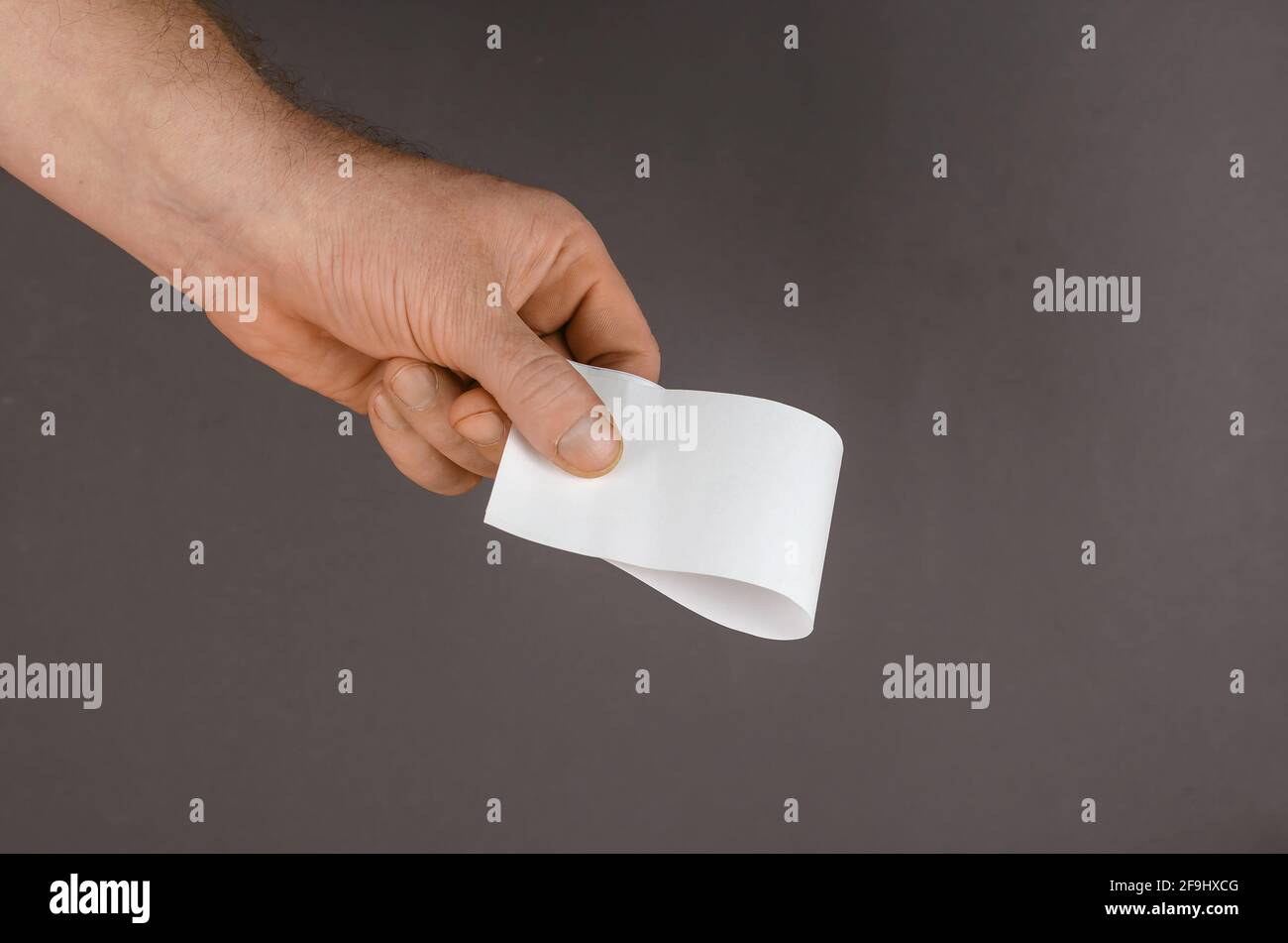 White piece of paper and right hand on gray background. Man holding a ...